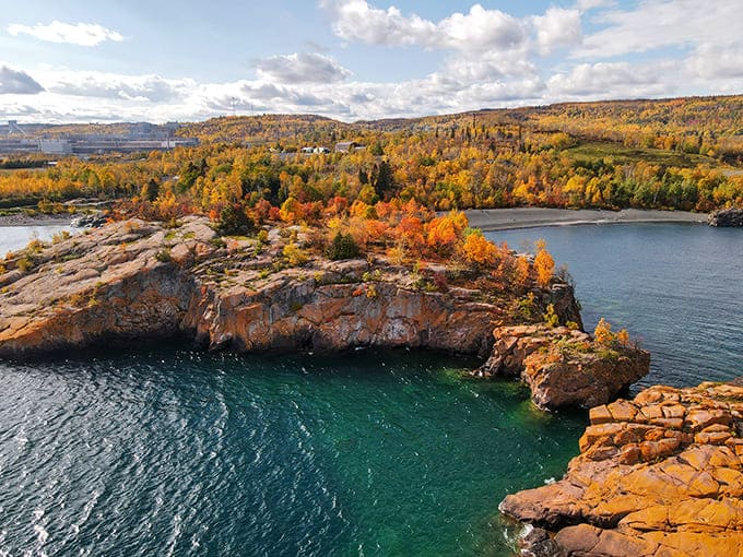 Autumn transforms the surrounding forest into a painter's palette, making the dark sand pop even more dramatically against the seasonal colors.