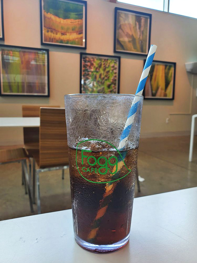 Even a simple soda becomes special at Fogg Café, served with a blue striped paper straw against a backdrop of botanical artwork.