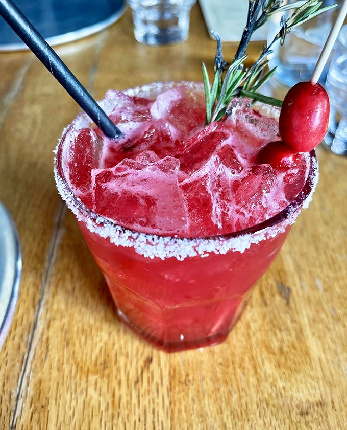 This vibrant cocktail, rimmed with sugar and garnished with fresh herbs, delivers the perfect balance of sweet and tart in every sip.