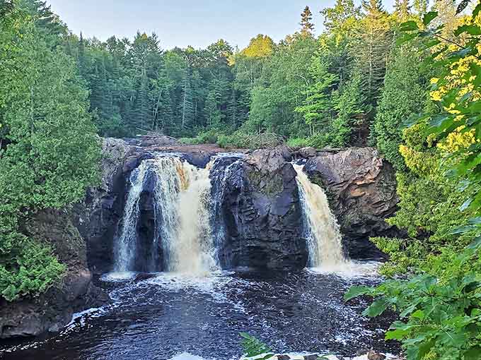 Big Manitou Falls plunges dramatically between forest-clad cliffs, its thundering waters creating a misty veil that dances in dappled sunlight.