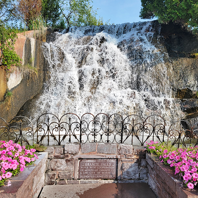Water cascades down in sheets of crystal clarity, framed by decorative ironwork and vibrant flowers &ndash; nature and human artistry in perfect harmony.