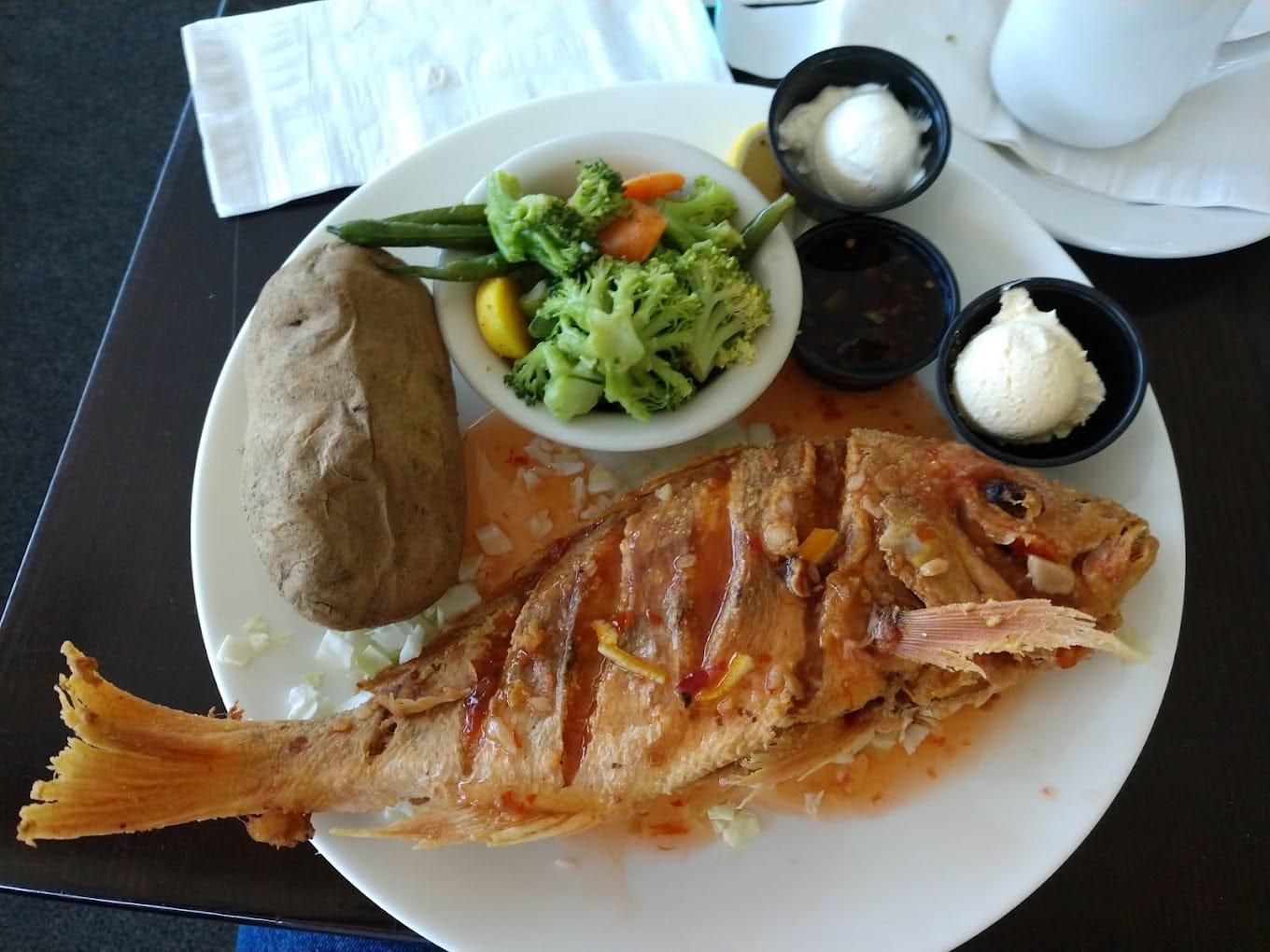 a full meal plate featuring a grilled fish with a side of vegetables and a baked potato