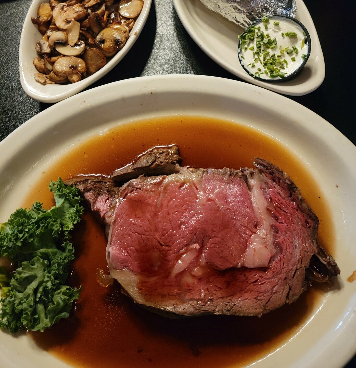 a hearty steak dinner complete with a baked potato and a side of saut&eacute;ed mushrooms