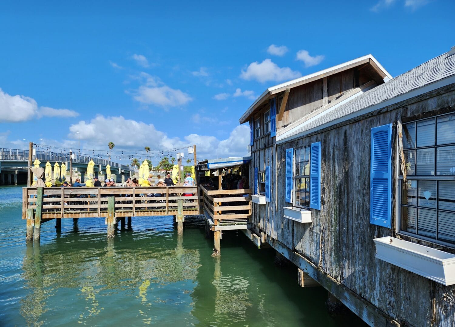 a rustic waterfront restaurant deck with patrons dining under yellow umbrellas overlooking a calm waterway