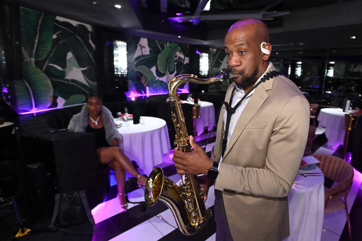 a saxophonist playing live music in a sophisticated restaurant with tropical wallpaper and a dimly lit ambiance