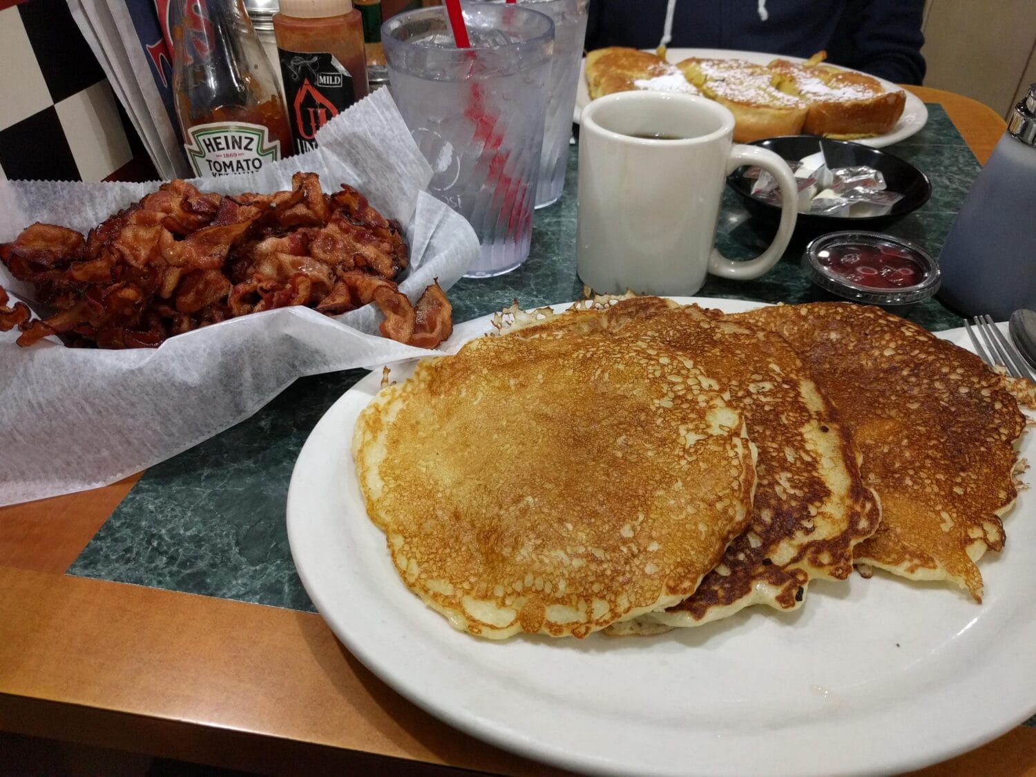 a table of breakfast dishes with a plate of pancakes bacon and french toast