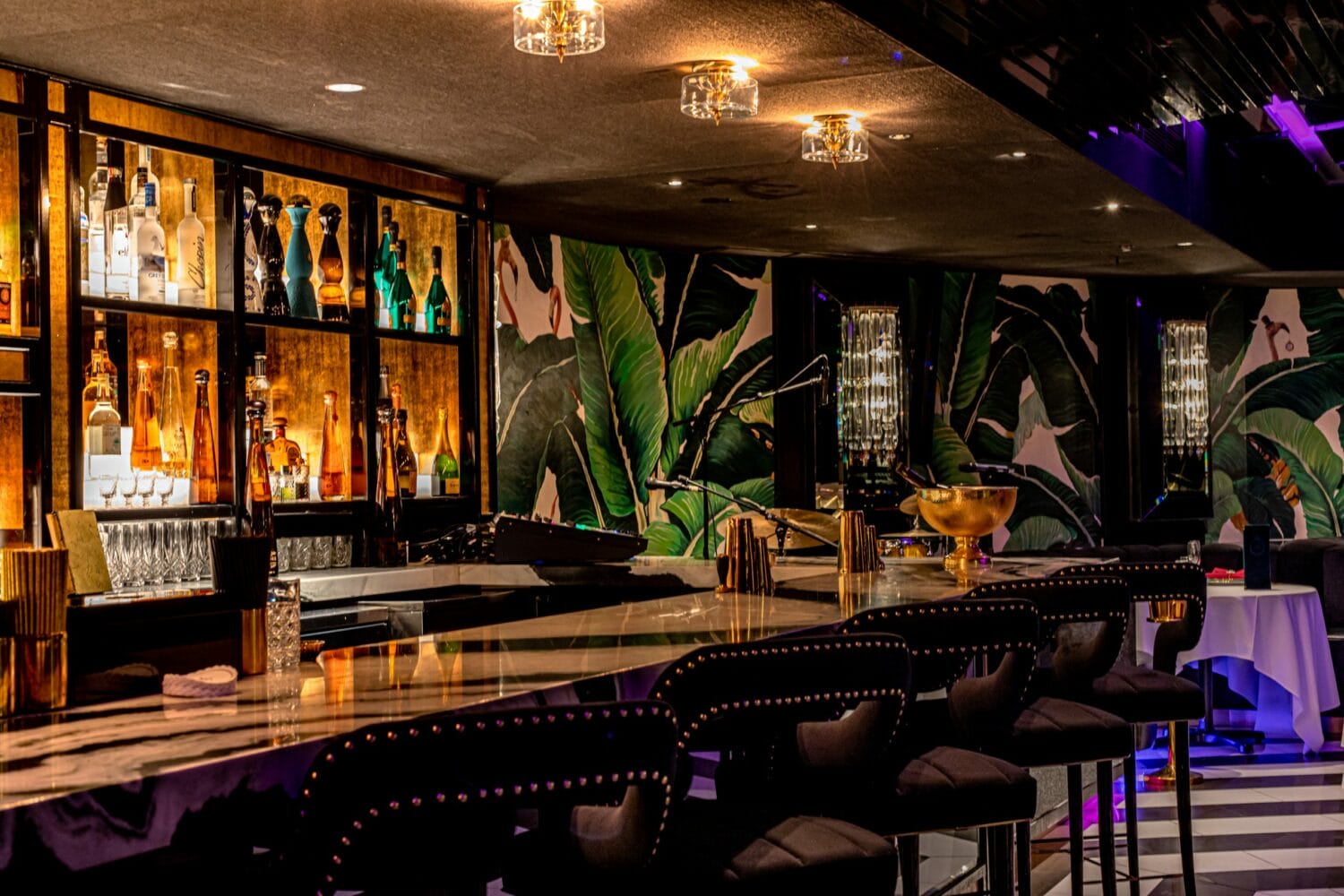 a trendy bar setting with a tropical wallpaper backdrop marble countertop and upholstered stools under warm ambient lighting