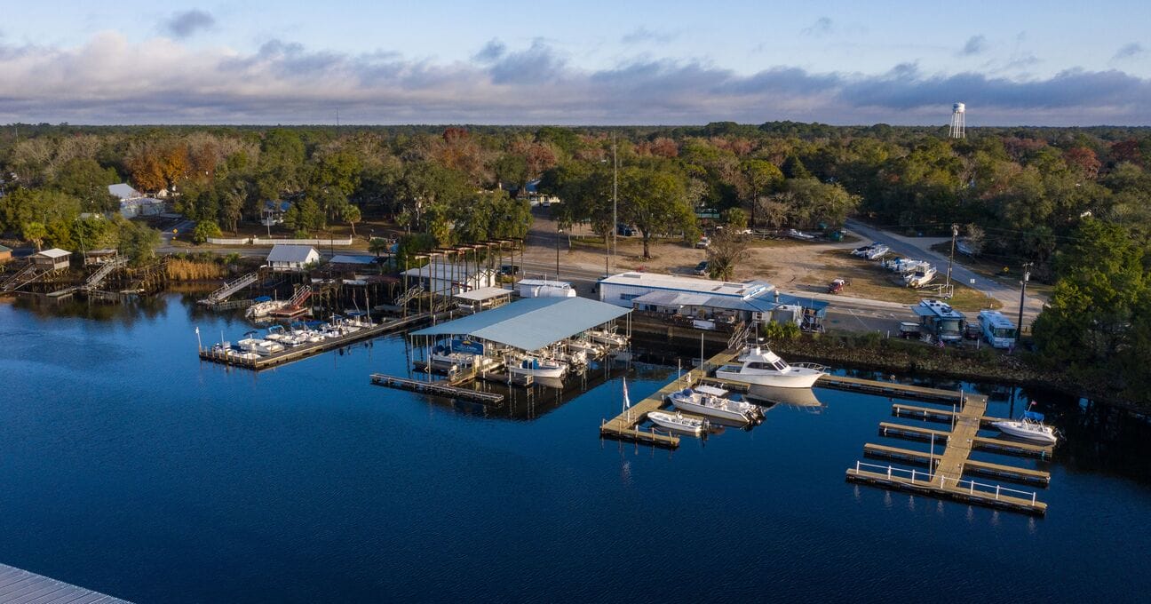 an aerial view of a marina with moored boats and surrounding facilities in a natural wooded environment