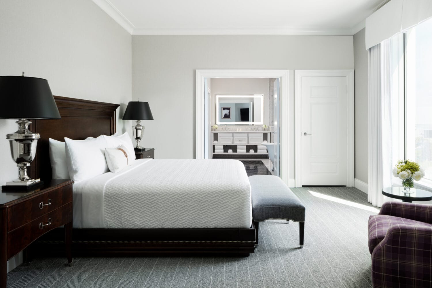 an elegant hotel room with large bed with plush bedding dark wood furniture