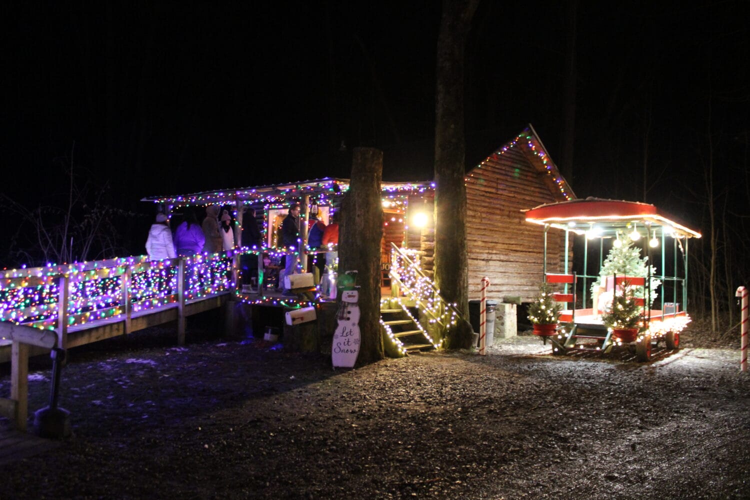 an enchanting nighttime scene with a well lit gazebo and a cheerfully decorated log cabin inviting families to enjoy the holiday spirit