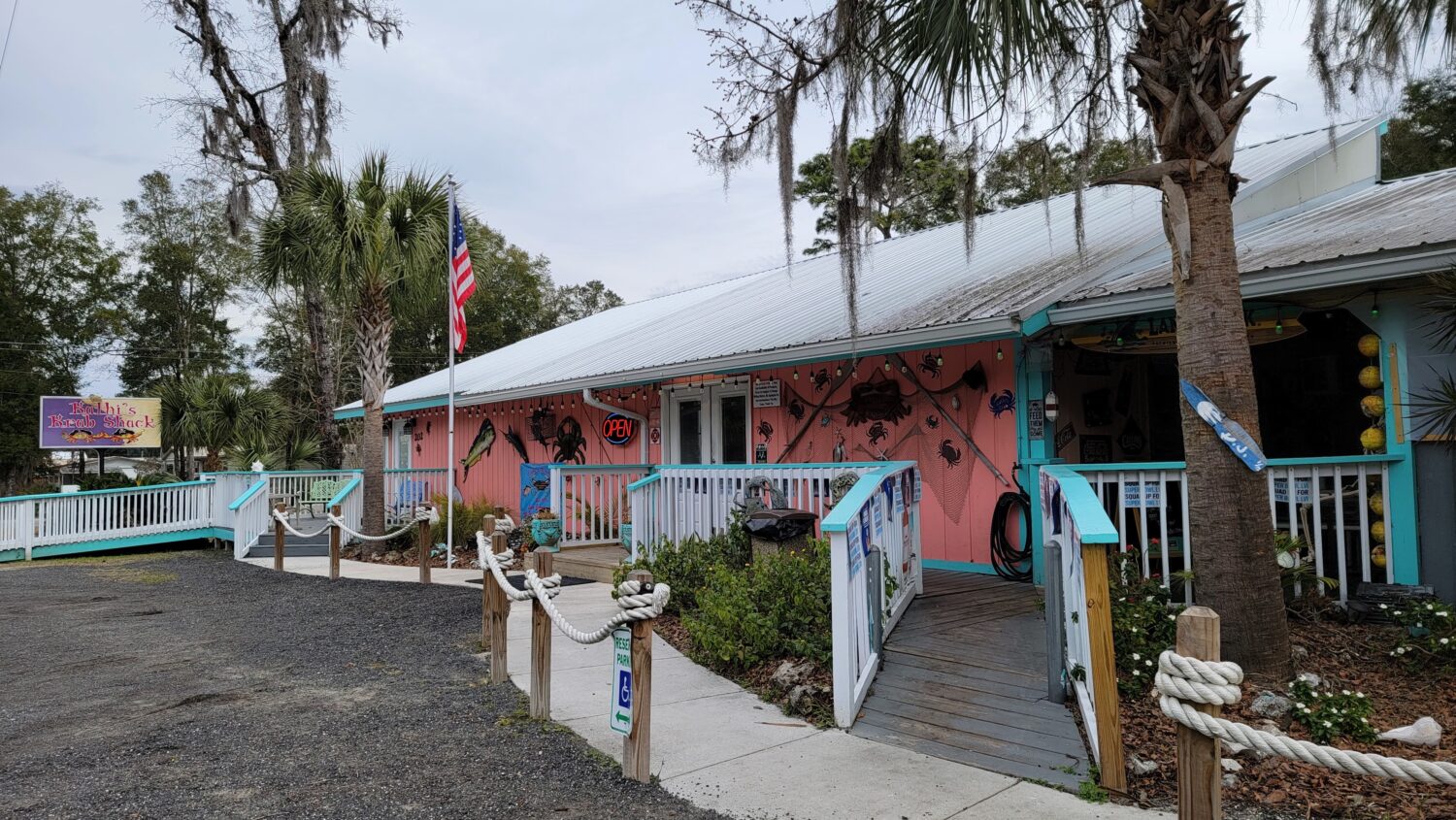 kathi's krab shack, a casual seafood restaurant, with a pink fa&ccedil;ade decorated with crab motifs and surrounded by lush palms and moss draped trees