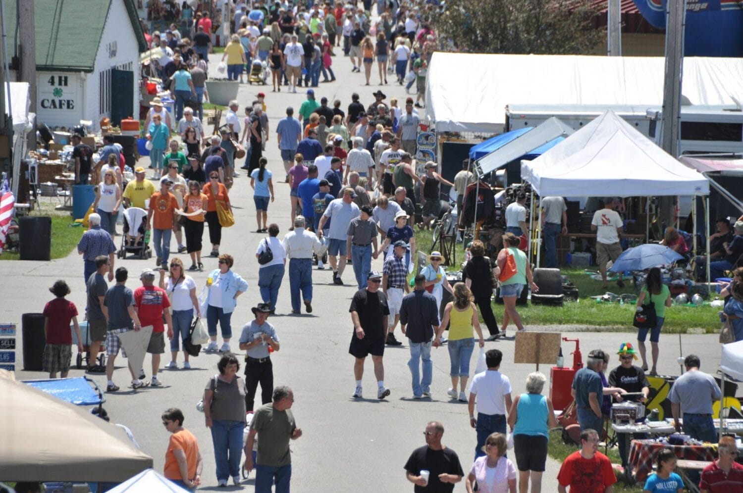 the flea market filled with people browsing through stalls and exhibits on a clear sunny day