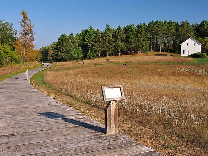 A wooden boardwalk winds through golden prairie grasses, leading to a historic white building &ndash; nature's red carpet to Minnesota's past.