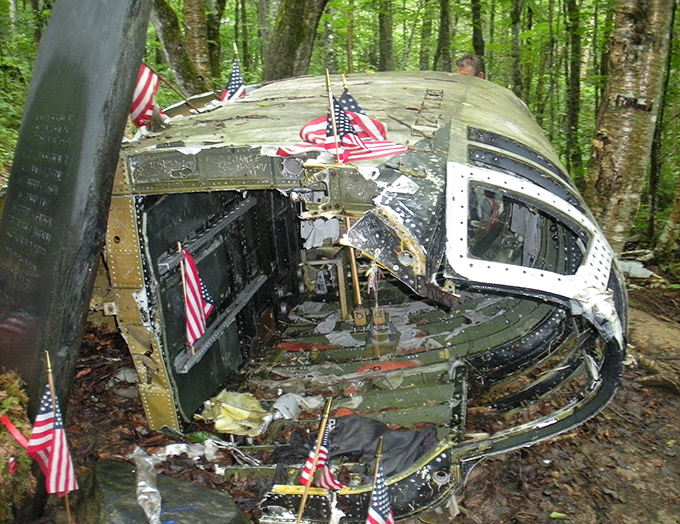 The weathered nose section of the B-52 rests among the trees, American flags standing sentinel over this solemn piece of history.