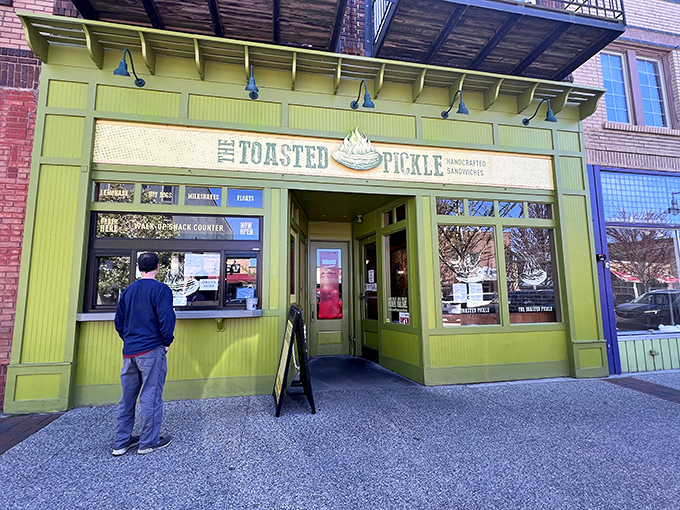 The vibrant lime-green exterior of The Toasted Pickle beckons pickle enthusiasts with its charming storefront and walk-up window in downtown Grand Haven.