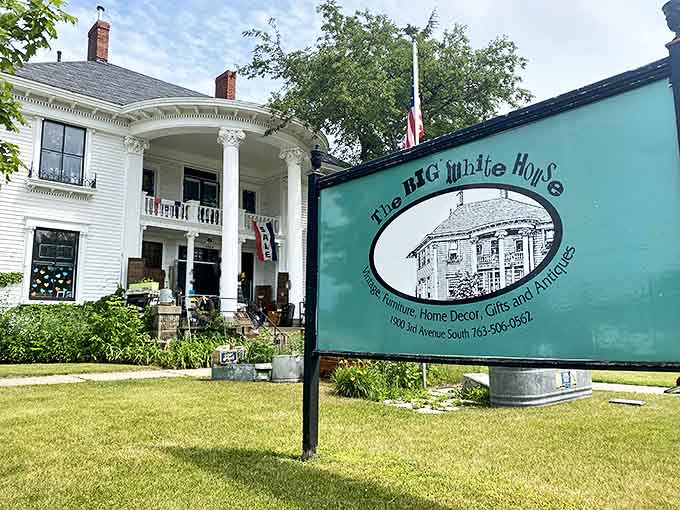 The stately white colonial mansion stands proudly with its grand columns and welcoming turquoise sign, promising treasures within.
