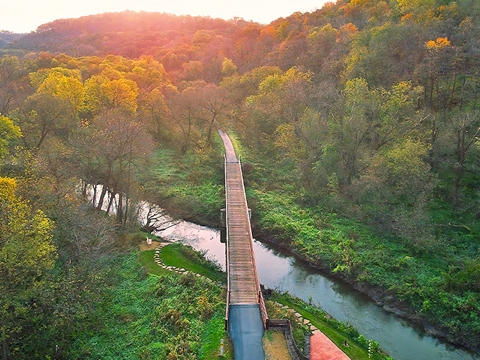 A wooden bridge stretches across the serene Cannon River, autumn colors painting the valley in golden hues at sunset.