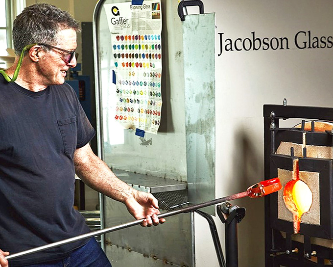 A master craftsman shapes molten glass with practiced precision, transforming raw material into art at Jacobson Glass Studio in Montville.