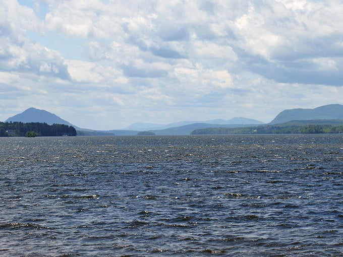 Rippling blue waters stretch toward distant mountains, where Vermont whispers secrets to Quebec across this international liquid border.