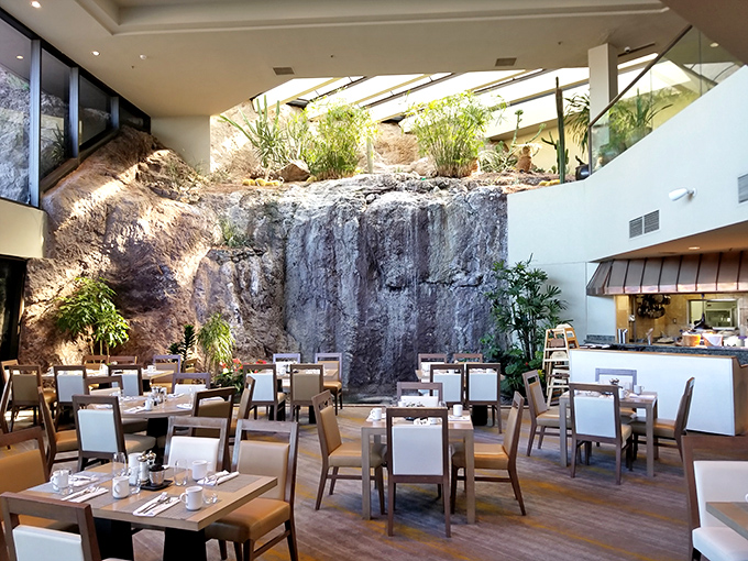 A dramatic indoor waterfall cascades down natural rock, creating nature's soundtrack for diners enjoying breakfast beneath the stone.