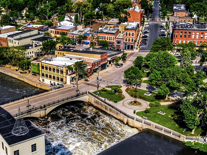 Aerial view of downtown Northfield where the Cannon River creates nature's Main Street, flowing beneath historic bridges and alongside charming brick buildings.