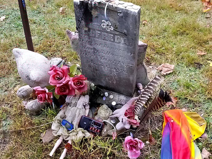 A weathered gravestone adorned with fresh flowers and mementos – visitors often leave tokens for those long passed, creating unexpected connections across centuries.