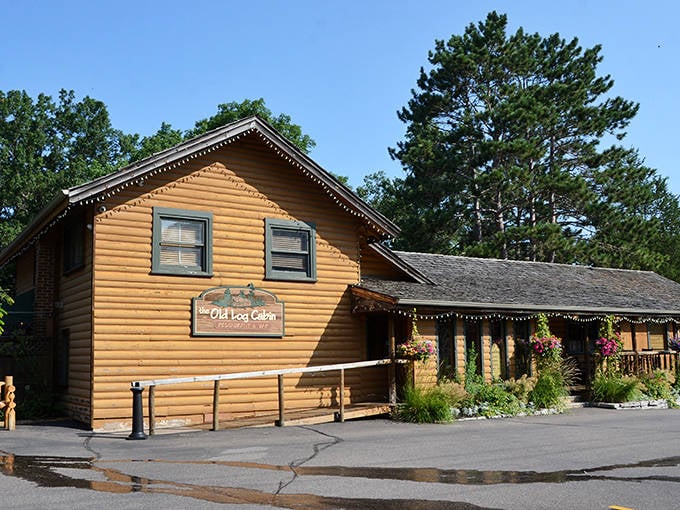 The golden-hued log exterior of The Old Log Cabin stands like a beacon of comfort food promise among towering Minnesota pines.
