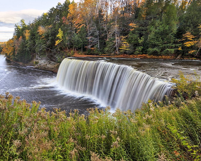 Tahquamenon's Upper Falls creates nature's perfect curtain, where 50,000 gallons per second take a dramatic 50-foot plunge through Michigan's autumn splendor.
