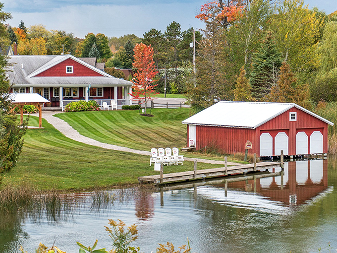A picture-perfect Michigan postcard: Boathouse Vineyards' iconic red structures reflect in Lake Leelanau's calm waters, framed by autumn's fiery display.
