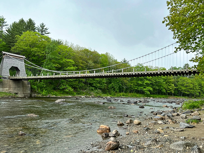 The Wire Bridge spans the Carrabassett River like a time traveler from the 1800s, its cables and wooden structure defying modern obsolescence.