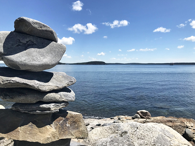 Someone's temporary stone sculpture stands in perfect equilibrium against the vast horizon, a human touch amid nature's grandeur.