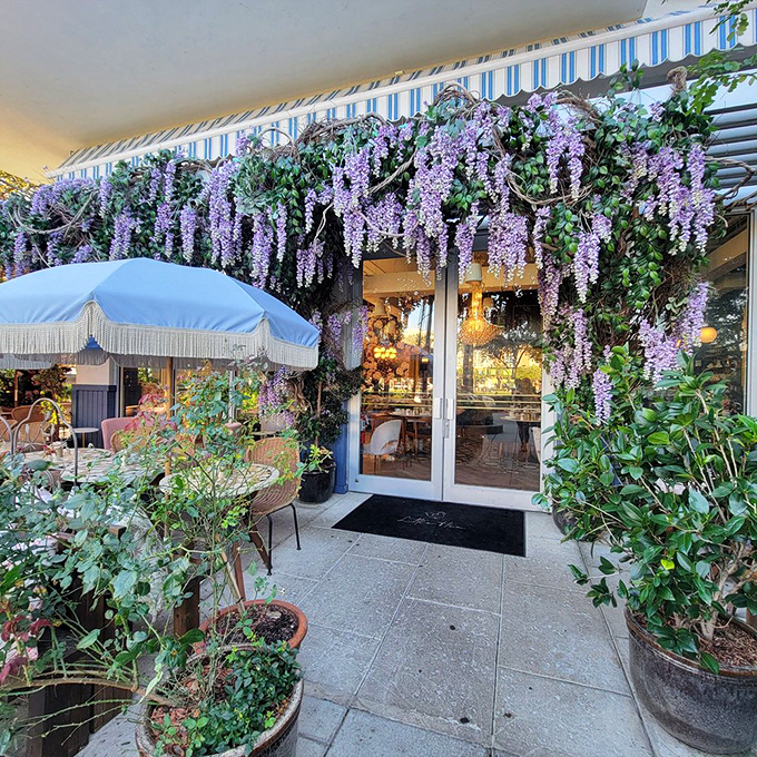 The entrance beckons with wisteria waterfalls and the promise of civilized indulgence. Those pink umbrellas aren't just shading tables&mdash;they're setting the mood.