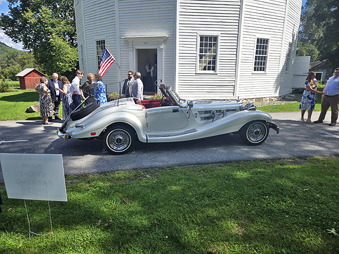 A classic car parked outside the church creates a timeless scene, bridging eras of American history in one perfect Vermont moment.