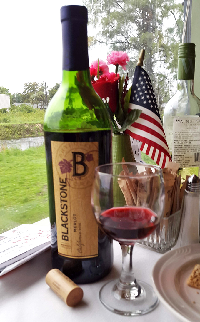 A glass of Blackstone Merlot catches the evening light, the perfect accomplice to both fine dining and criminal investigation.