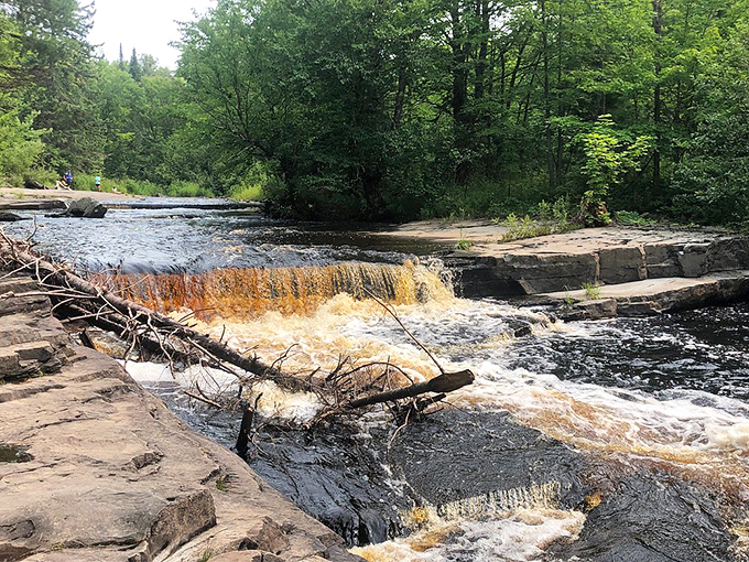 Rusty-hued waters cascade over ancient rock shelves, the river's mineral-rich waters painting the landscape in earthy watercolors.