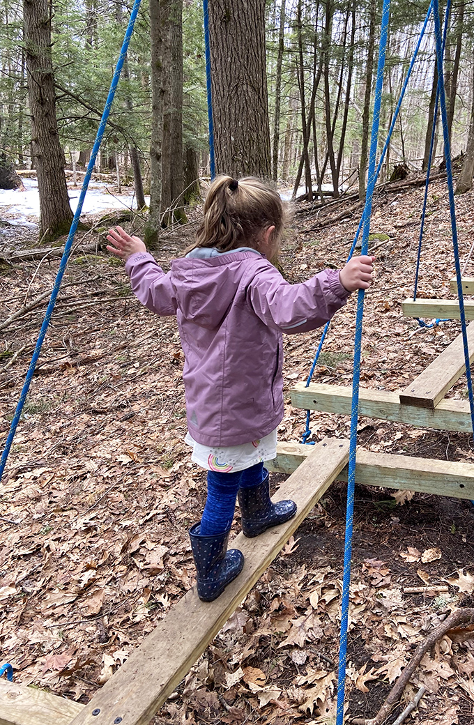 A child tests her balance on a simple rope bridge, finding joy in this woodland playground away from screens.