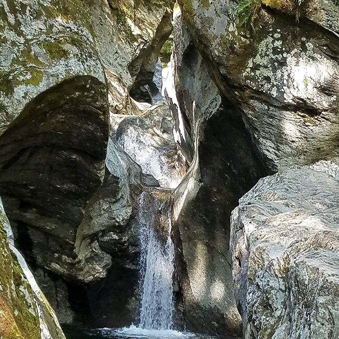 Water rushes through the narrow gorge, carving smooth rock walls shaped by centuries of flowing force.