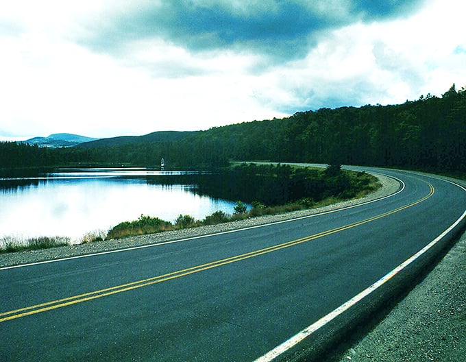 A smooth bend on Route 17 follows the quiet shoreline, reflecting peaceful skies and surrounding evergreens along this lakeside drive.