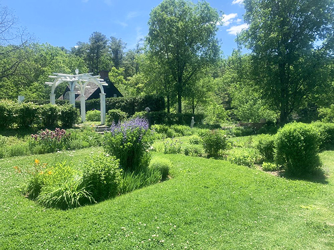 Colorful flowers and lush greenery fill the gardens at Vaughan Woods, where a white arbor and bright sunshine create a beautifully inviting scene.