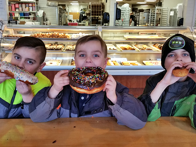 Young pastry enthusiasts demonstrate the proper technique for appreciating oversized baked goods, facial expressions clearly indicating successful flavor discoveries happening in real time.