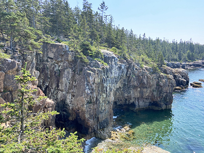 Sunlight plays across weathered cliffs, highlighting every crevice and curve of Maine's ancient granite shoreline in golden detail.