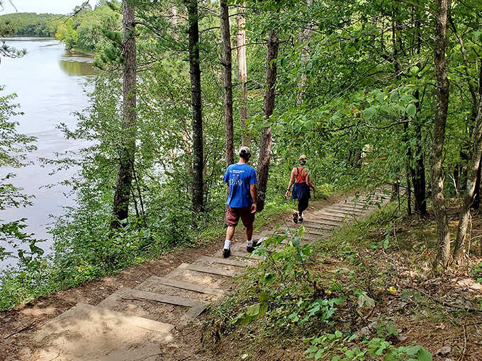 Hikers descend wooden steps toward the riverbank, demonstrating that sometimes the best path forward involves going down first.