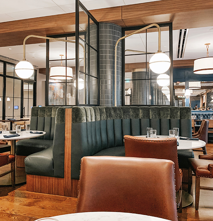 Plush green booths and sleek dividers create intimate dining pockets within the larger space, perfect for conversation and connection.