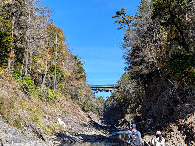Adventurous visitors explore the gorge from below, their presence providing scale to the massive walls of ancient stone rising around them.