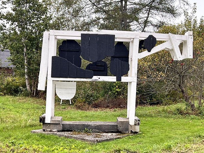 This wooden cow sculpture stands in silent contemplation, its geometric black and white form creating striking contrast against the green landscape.