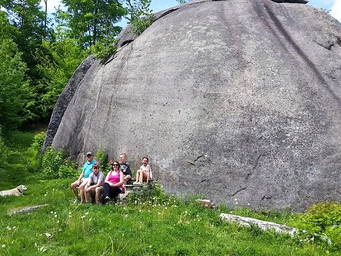 Visitors gather at the base of this natural wonder, their small figures emphasizing the immense scale of Maine's largest glacial erratic.
