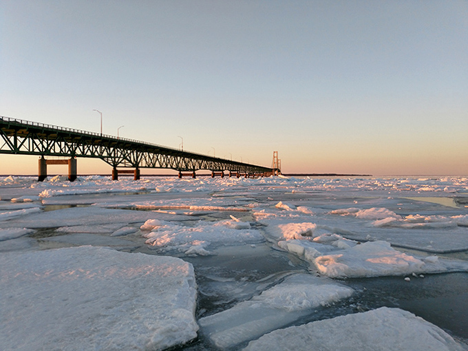 Even as winter ice claims the straits, the Mackinac Bridge maintains its vital connection, the setting sun painting its western face with golden light.