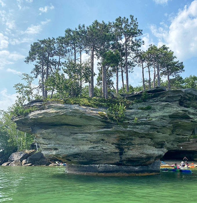 The rock's weathered texture reveals its geological biography – layers of ancient sediment compressed into stone, then artfully carved by endless waves.