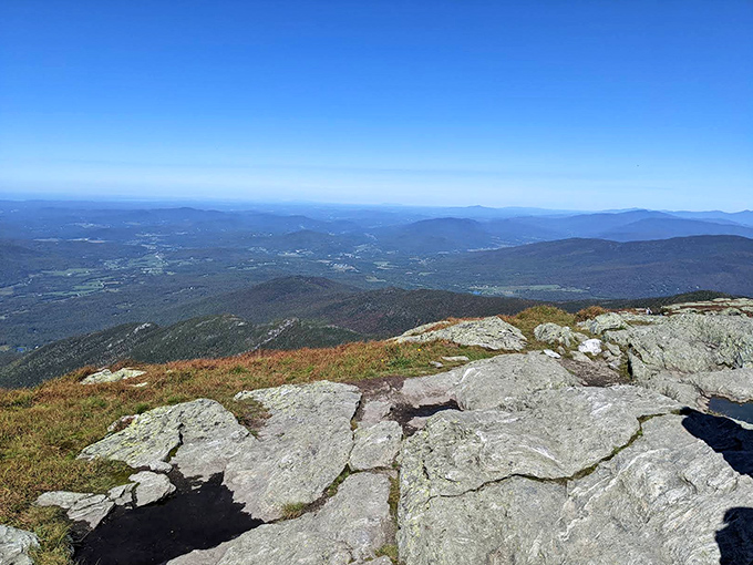 From this rocky perch, the world unfolds in layers of blue-tinged mountains, each ridge fading into the horizon like watercolor washes.