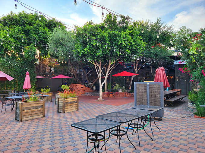Lush greenery surrounds the outdoor dining area, where red umbrellas pop against brick pavers in this urban garden escape.
